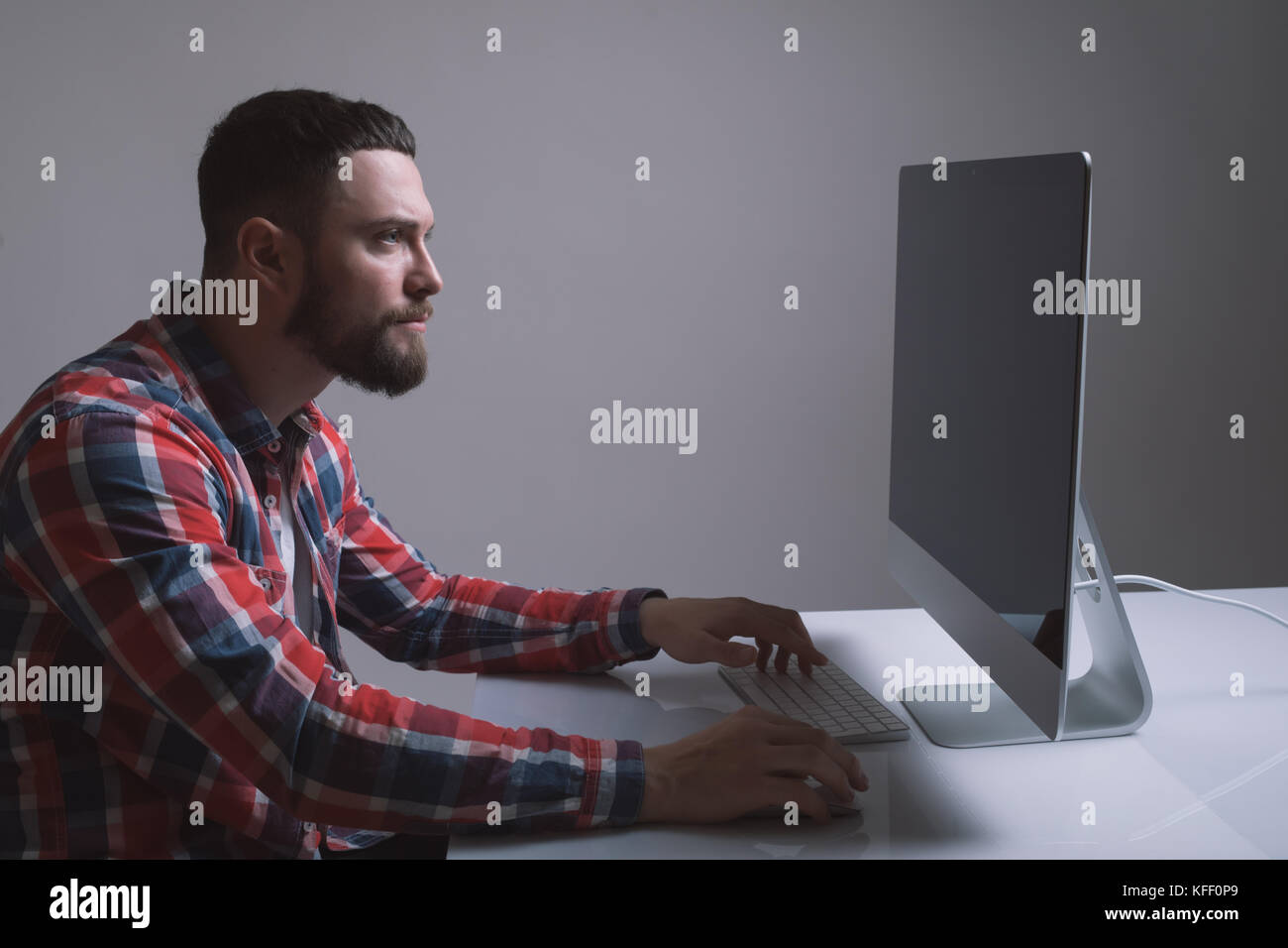 A bearded caucasian man is sitting behind the monitor of the computer ...