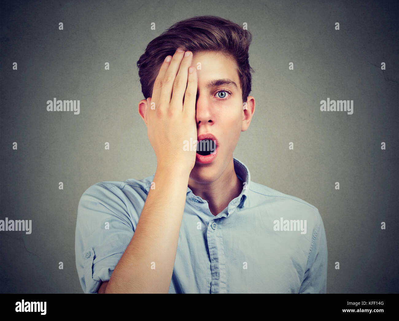 Surprised man, with one eye, covered by hand looking at camera isolated ...
