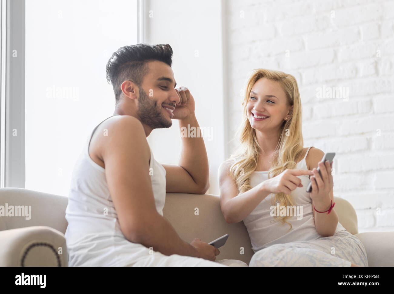 Young Beautiful Couple Sit On Coach Near Window, Using Cell Smart Phone ...