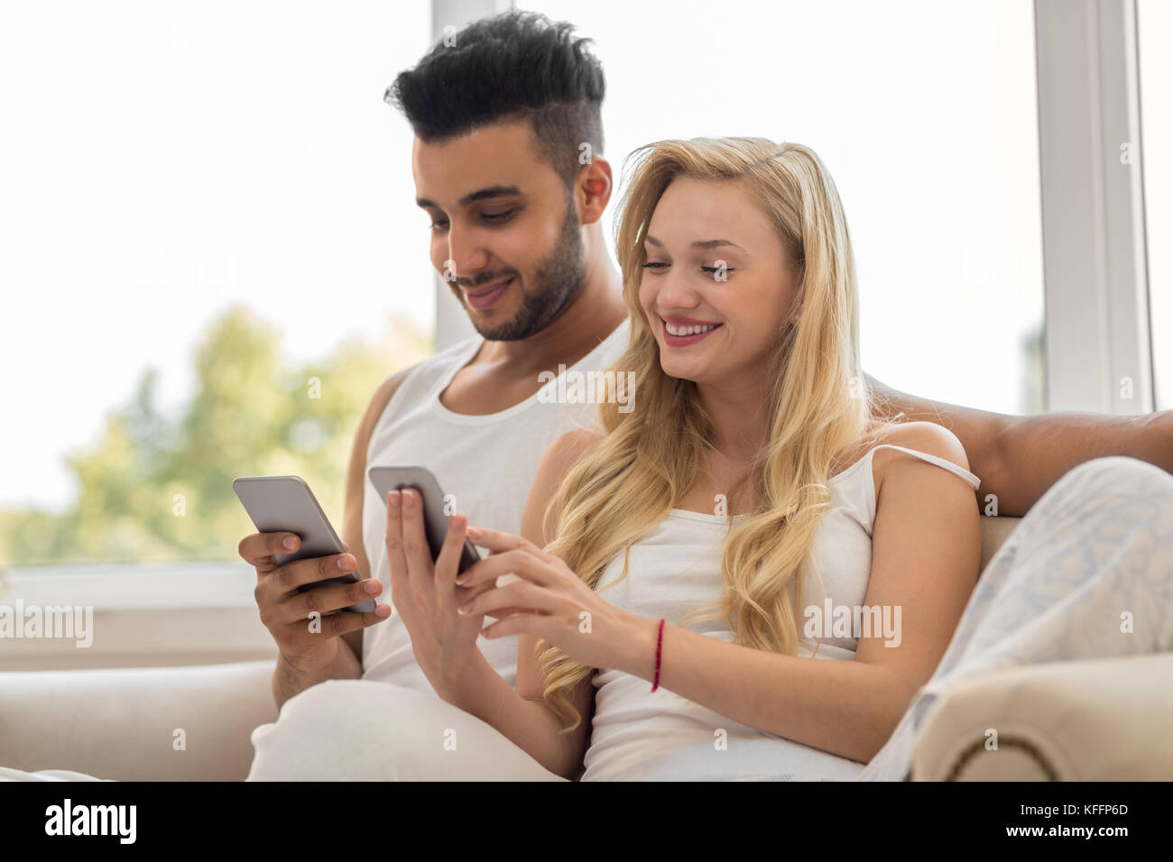 Young Beautiful Couple Sit On Coach Near Window, Using Cell Smart Phone ...