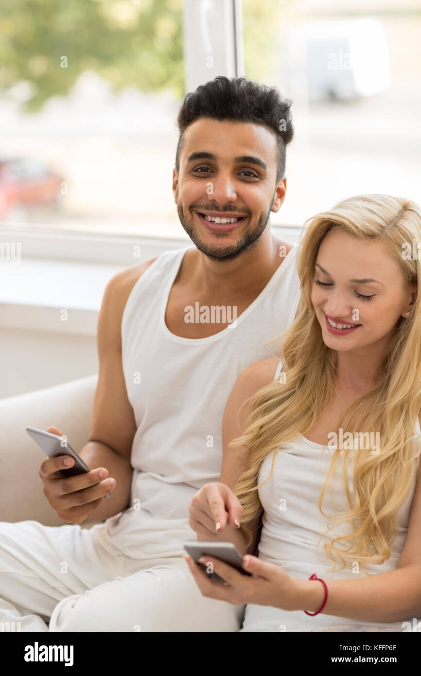 Young Beautiful Couple Sit On Coach Near Window, Using Cell Smart Phone ...