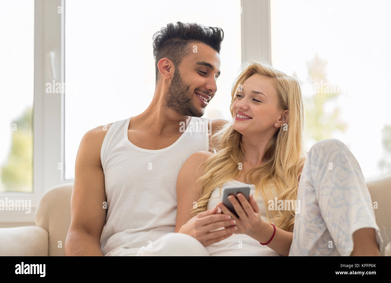 Young Beautiful Couple Sit On Coach Near Window, Using Cell Smart Phone ...