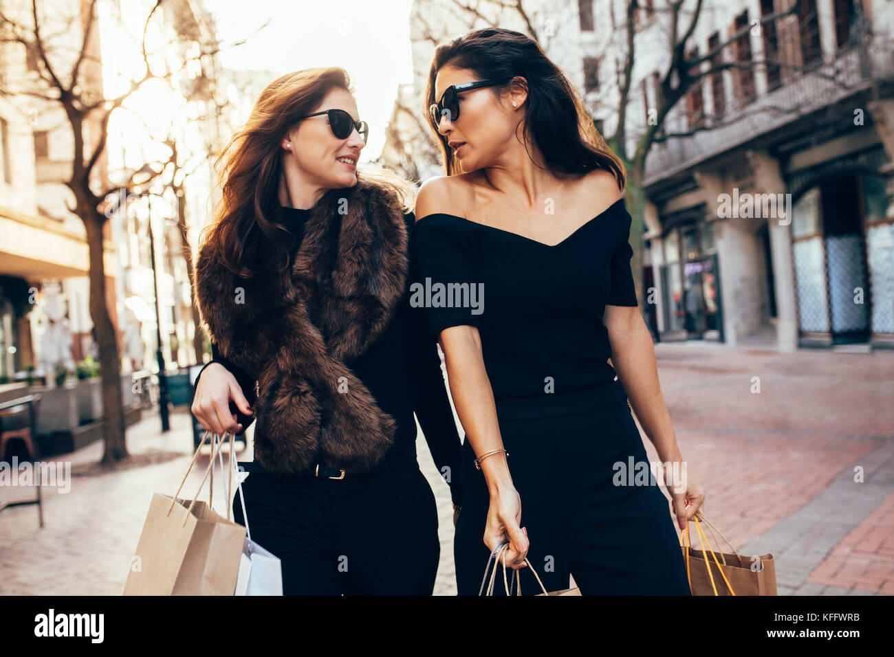 Women with shopping bags walking along the city street. Female shoppers ...