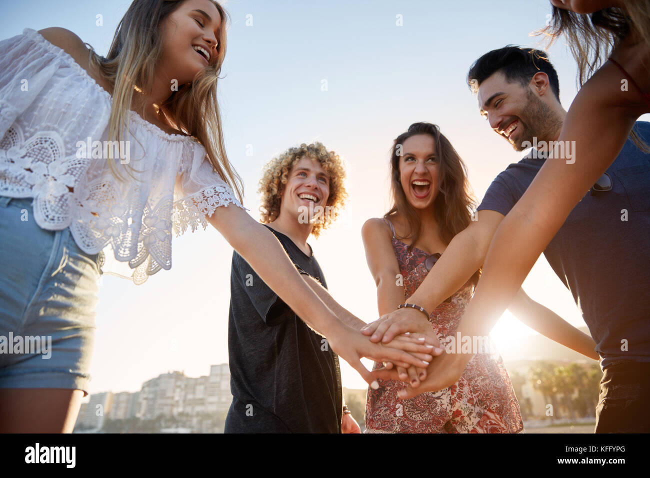 Portrait of happy friends holding hands together in sunlight laughing ...