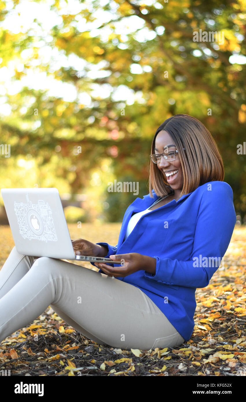 A black women using a laptop computer in a park on a beautiful fall day ...