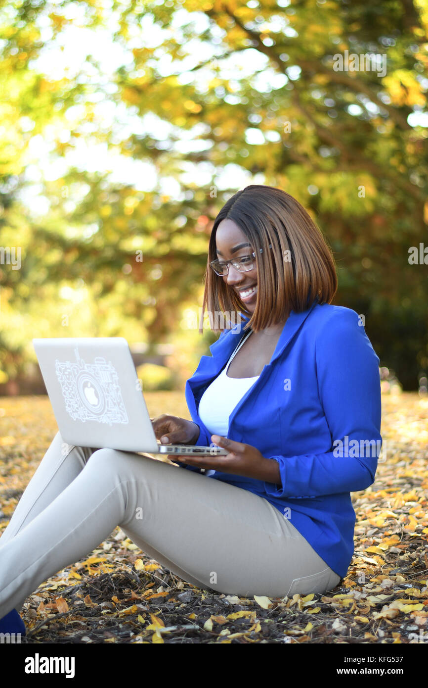 A black women using a laptop computer in a park on a beautiful fall day ...
