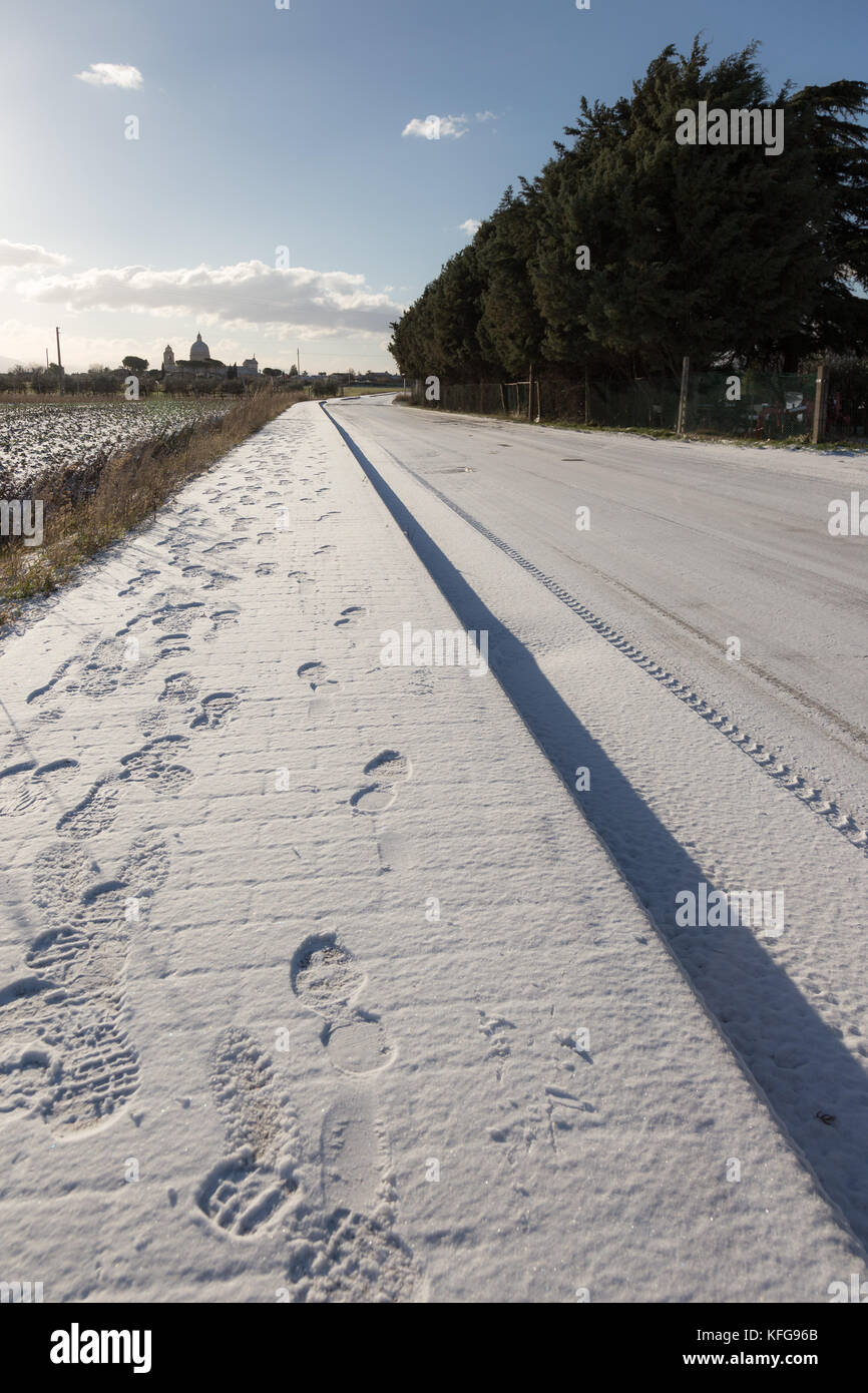 Many footprints on a sidewalk covered by snow near a long road, on a ...