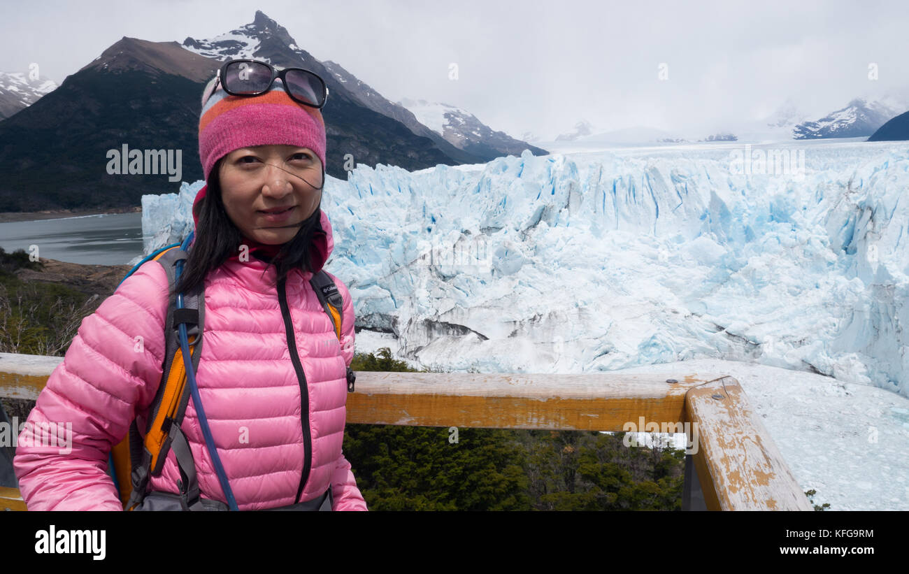 Young Asian traveler standing on glacier visitor walkway in pink jacket ...
