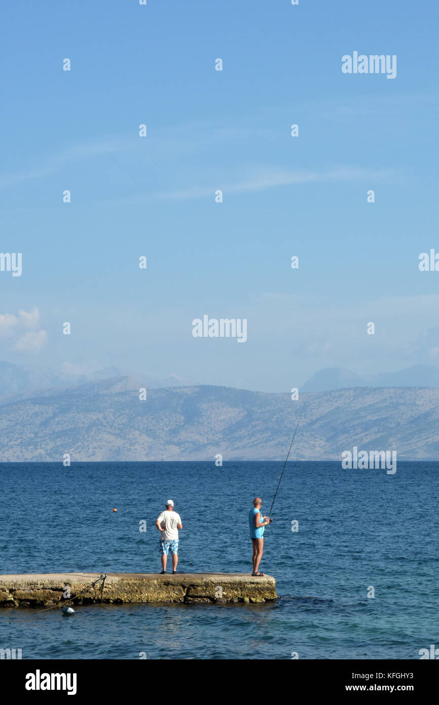 Two men standing on a small stone pier jetty fishing with rods on the ...