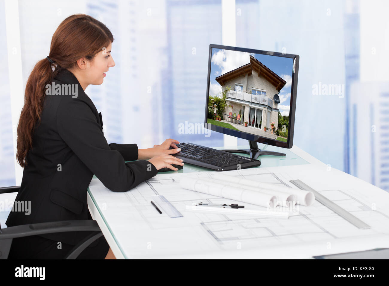 Side view of young female architect surfing house on computer at desk ...