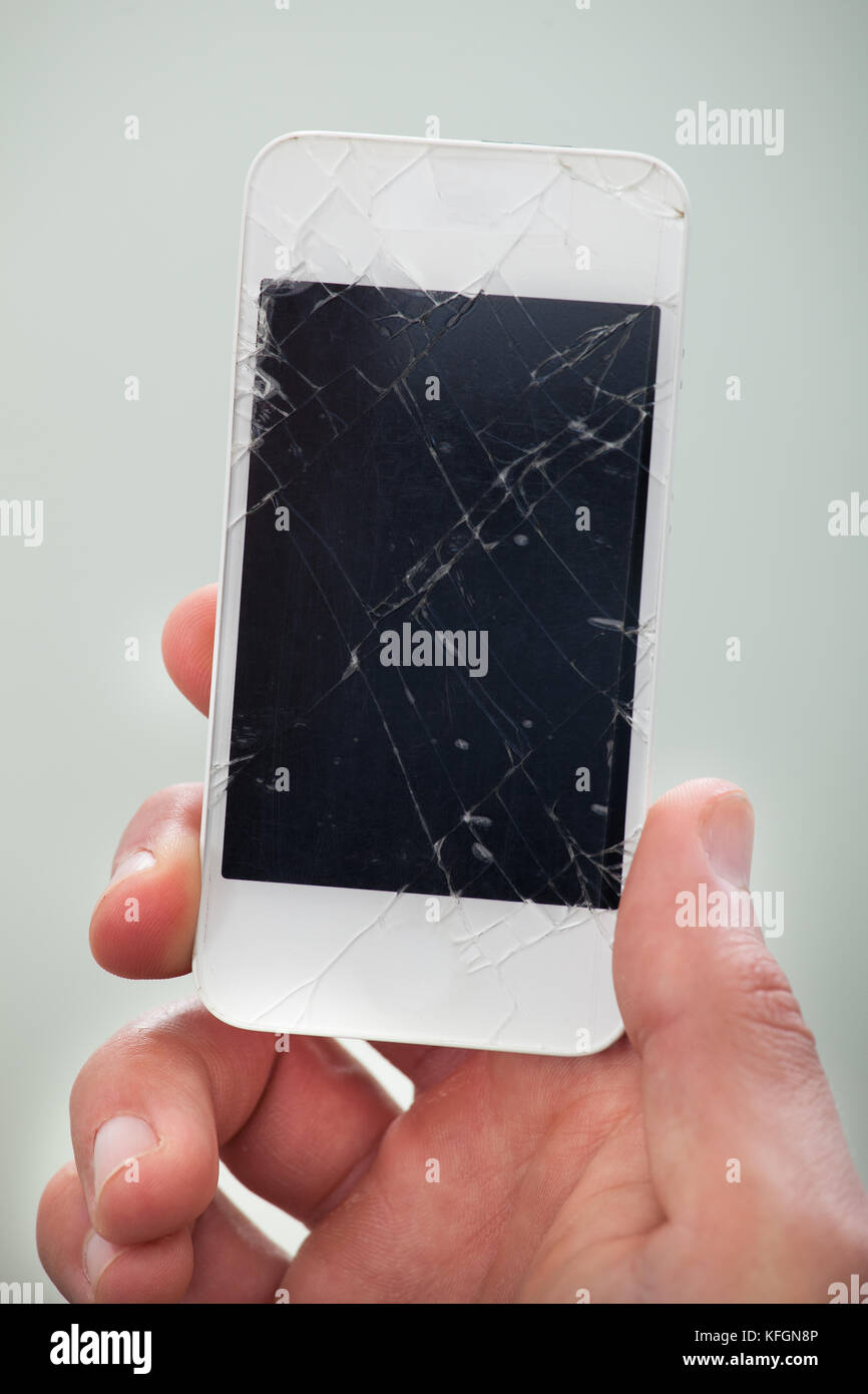 Businessman holding a damaged smartphone with a smashed screen in his ...