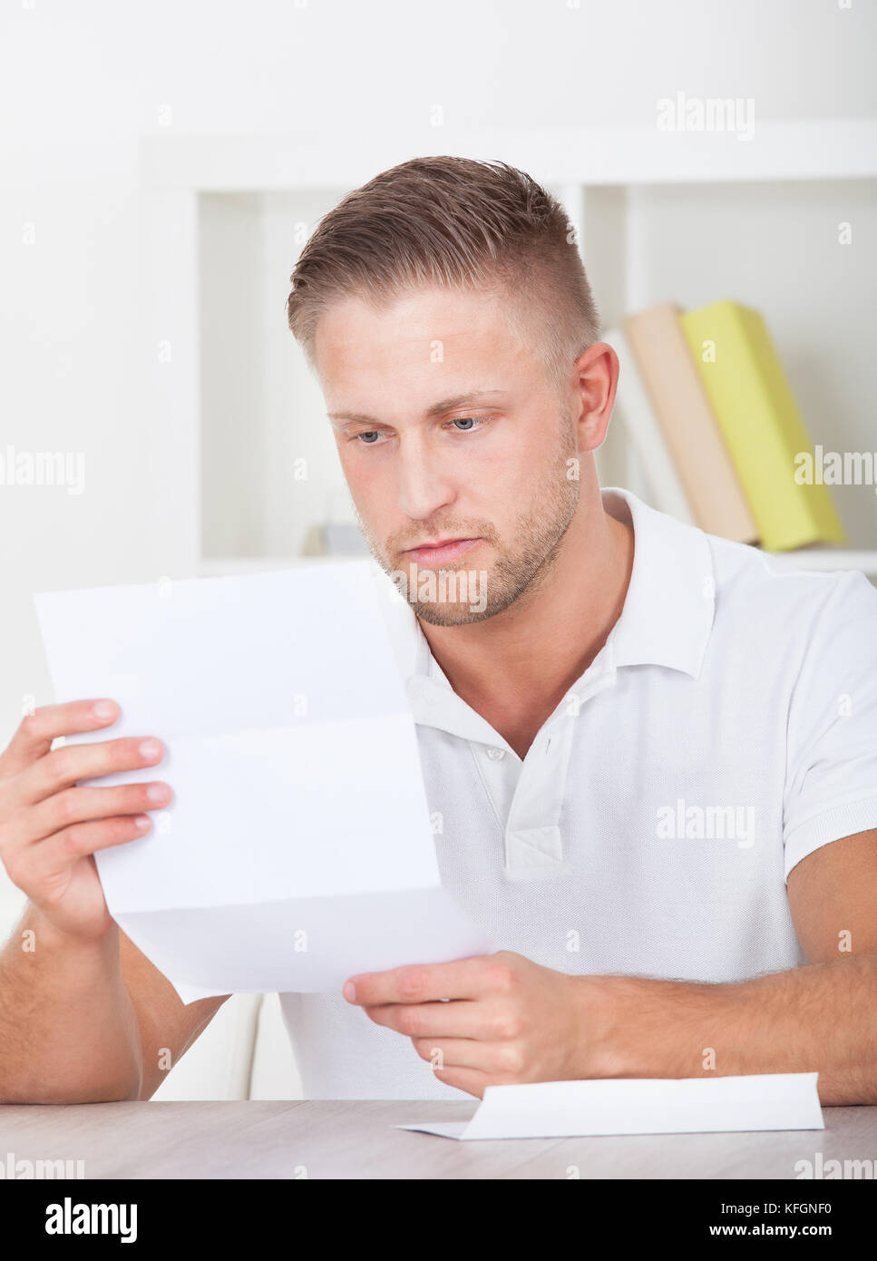 Man sitting reading a letter in an office with a serious expression ...