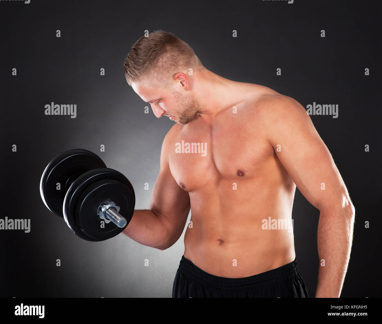 Muscular shirtless young man lifting weights in a gym as he works out ...