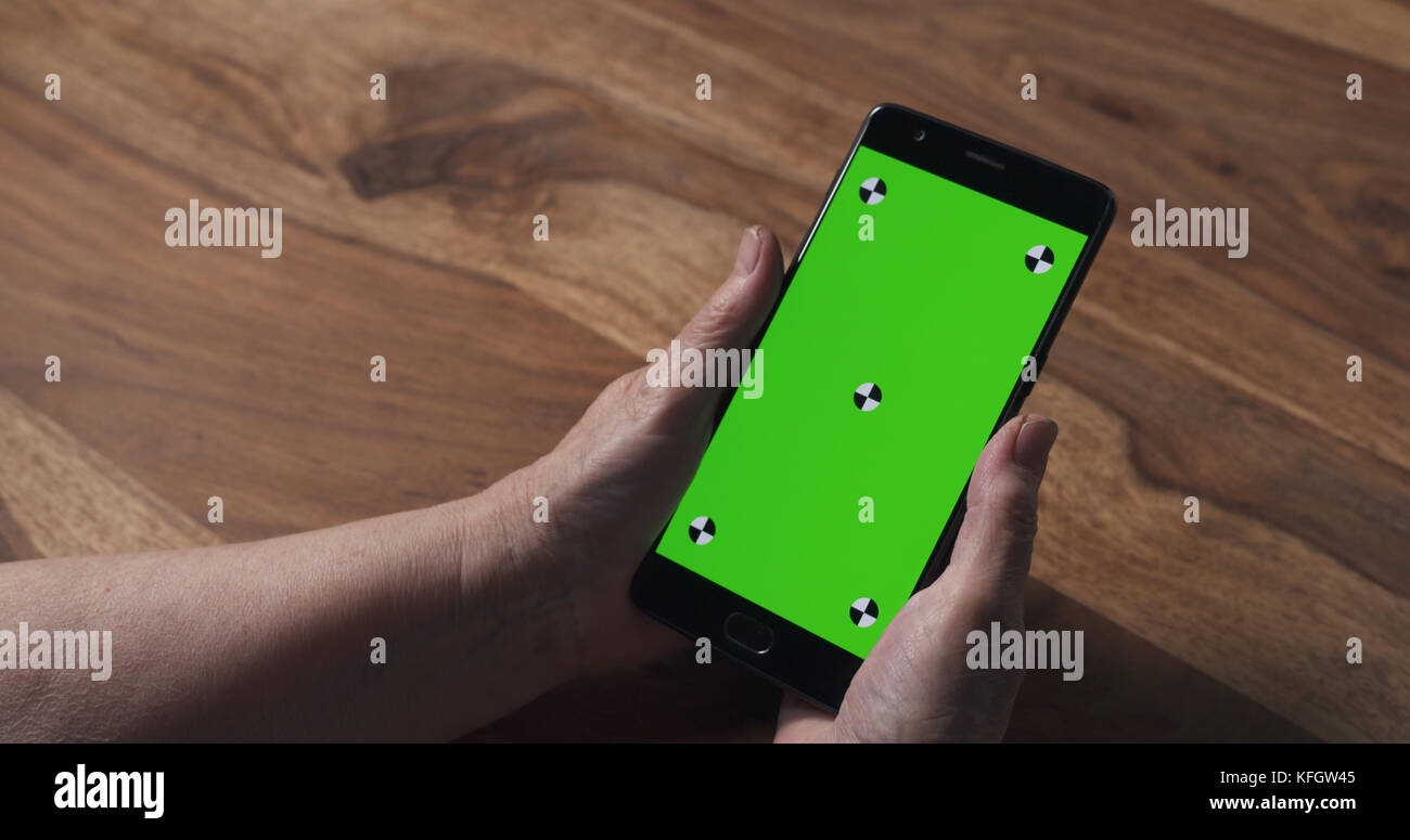 old female hands holding smartphone with green screen over wood table ...