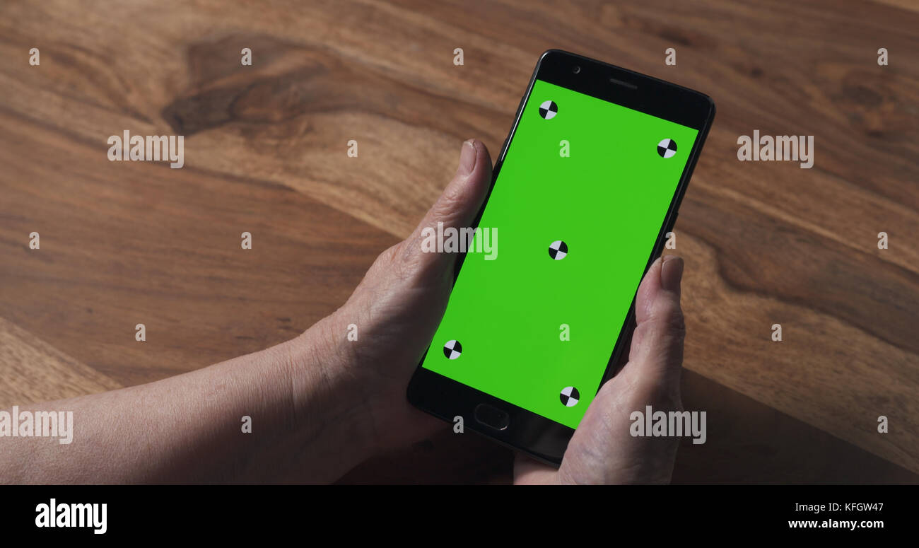 old female hands holding smartphone with green screen over wood table ...
