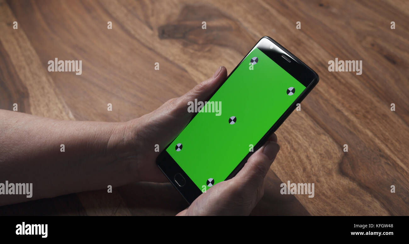 old female hands holding smartphone with green screen over wood table ...