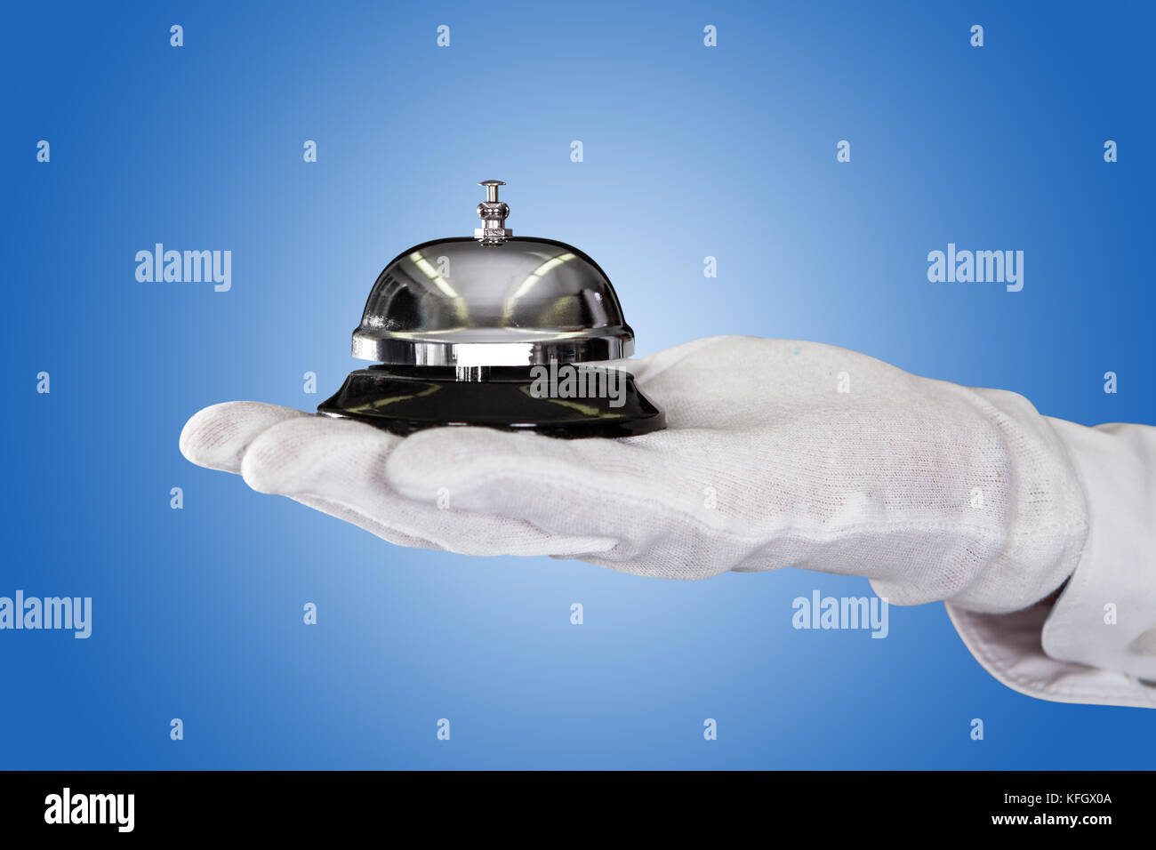Closeup of butler's hand holding service bell against blue background ...