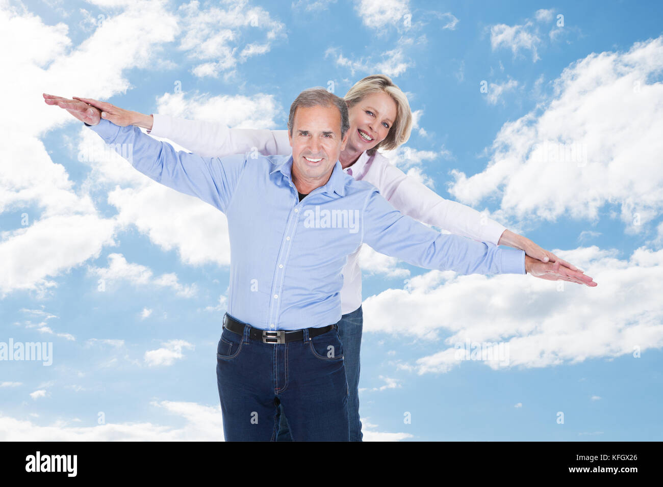 Portrait of happy couple with arms outstretched standing against cloudy ...