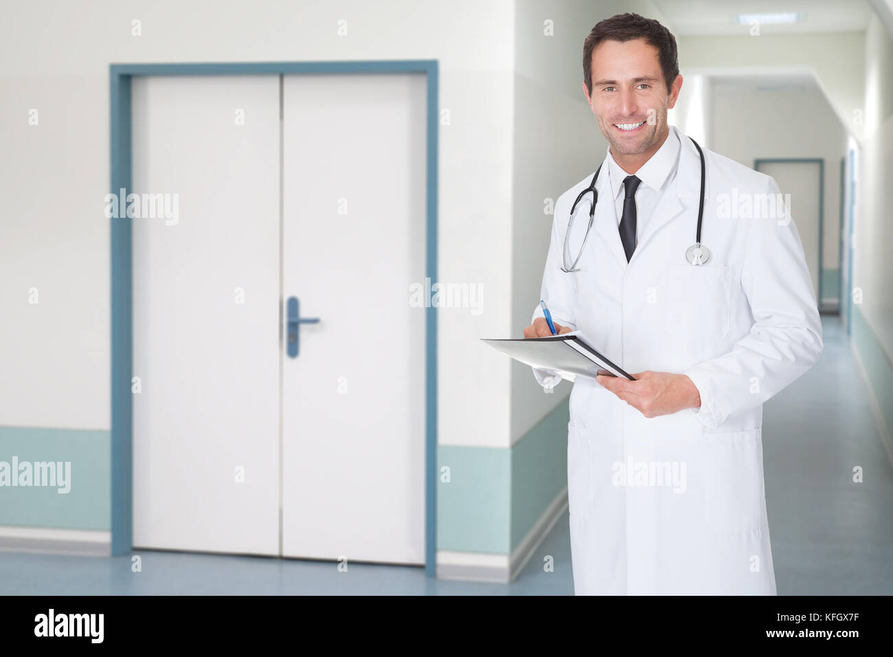 Portrait of happy confident doctor holding file in hospital corridor ...