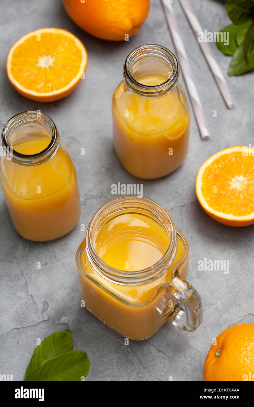 orange juice in a mason jar, glass bottles, fresh oranges on a gray ...