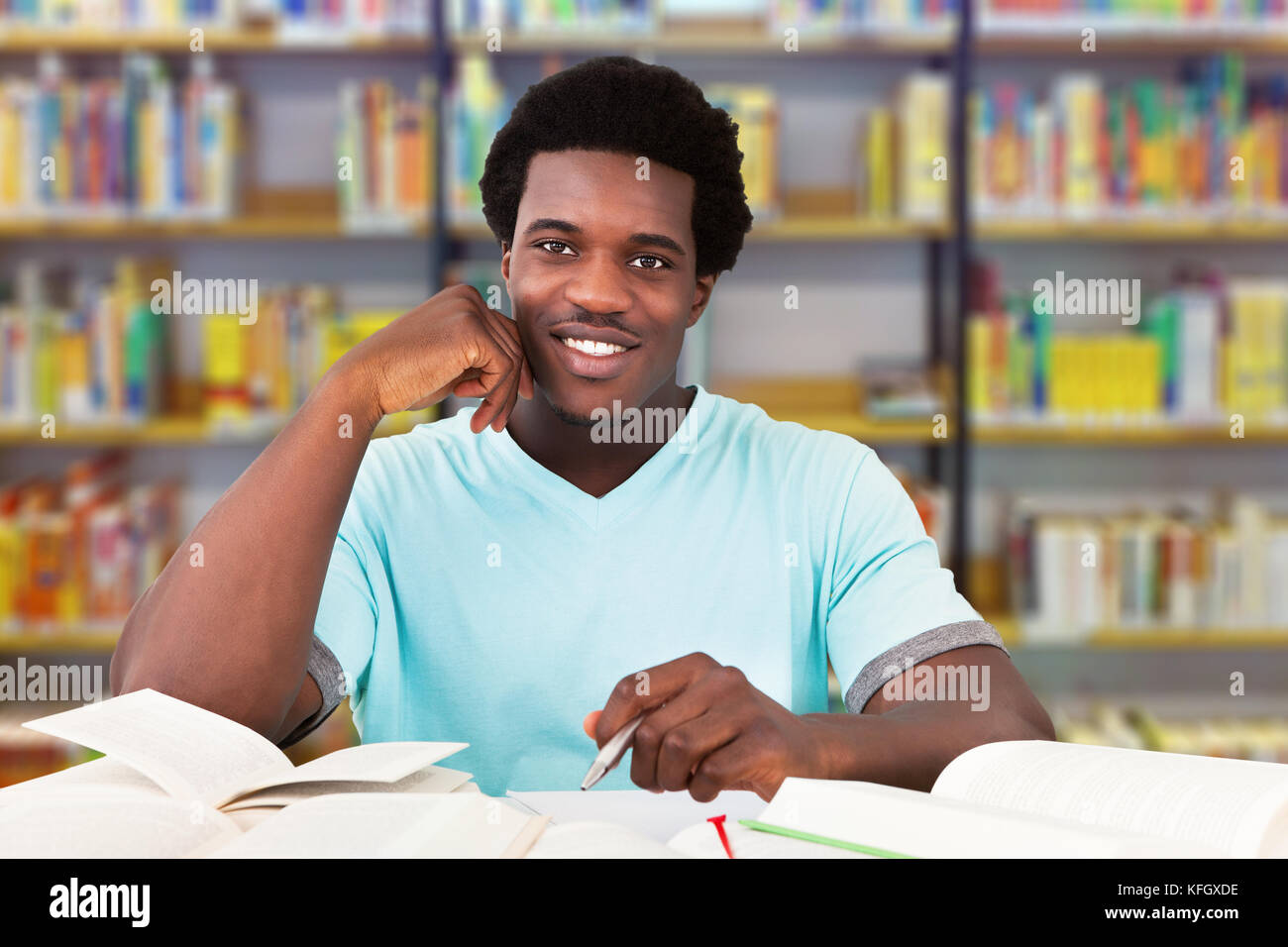 Portrait of smiling male university student studying at table in ...