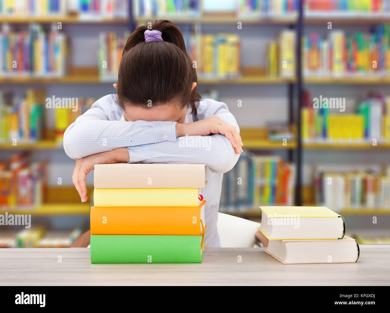 Tired female college student leaning on stack of books at desk in ...