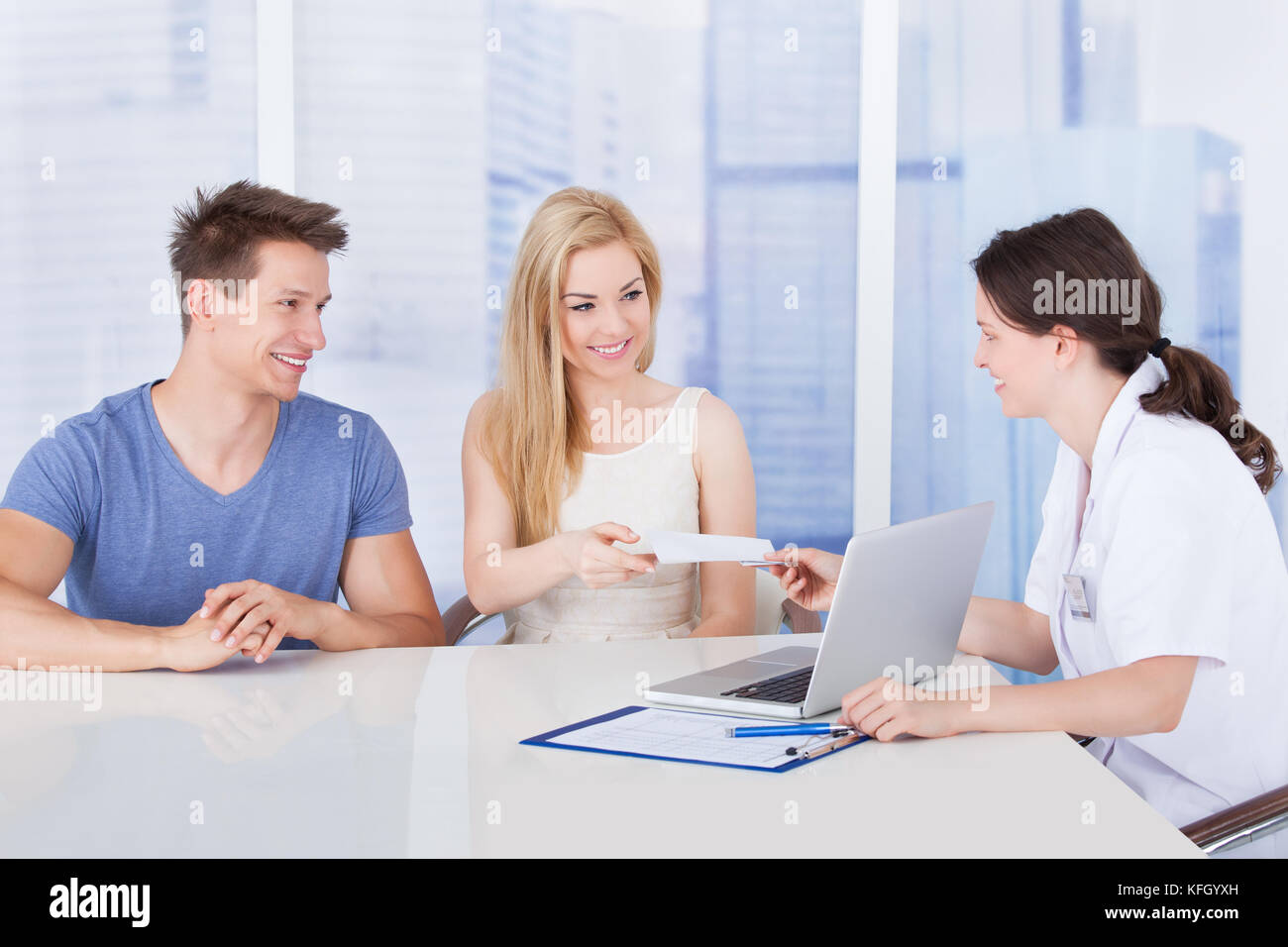 Female doctor giving prescription paper to young couple at desk in ...