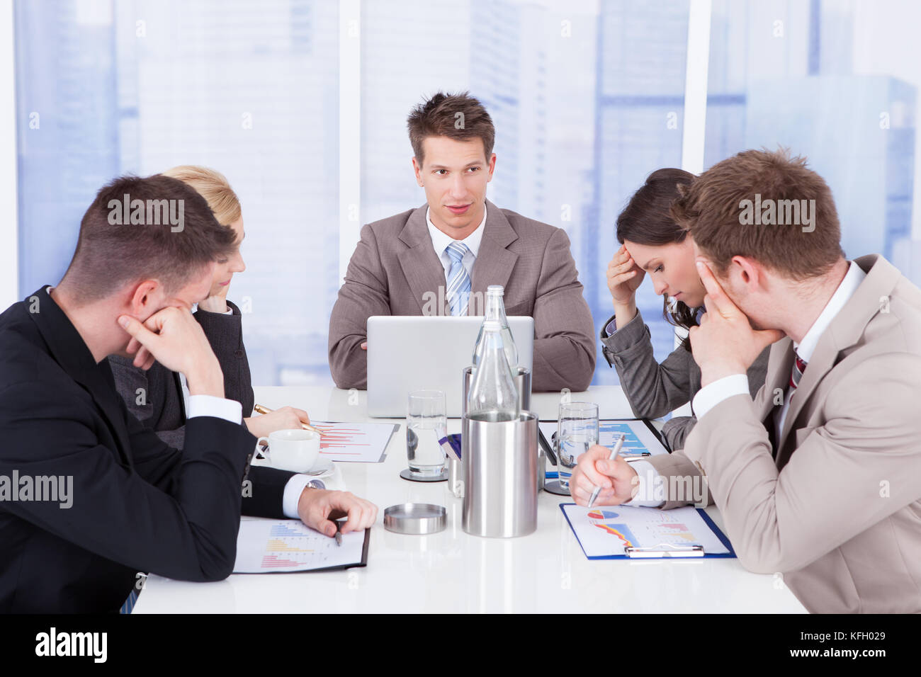 Young businessman looking at tired colleagues during conference meeting ...