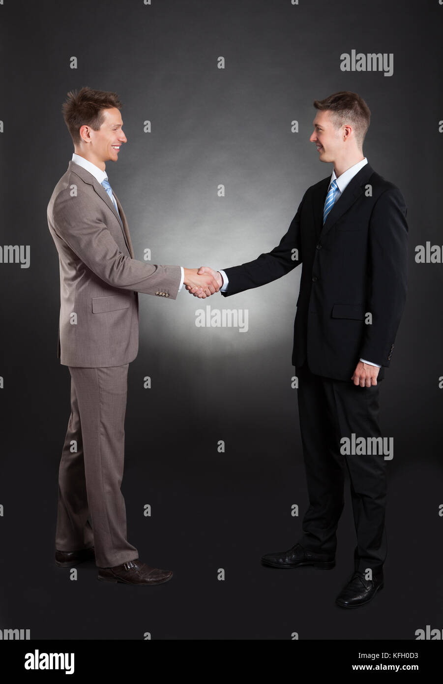 Full length of smiling businessmen shaking hands against black ...