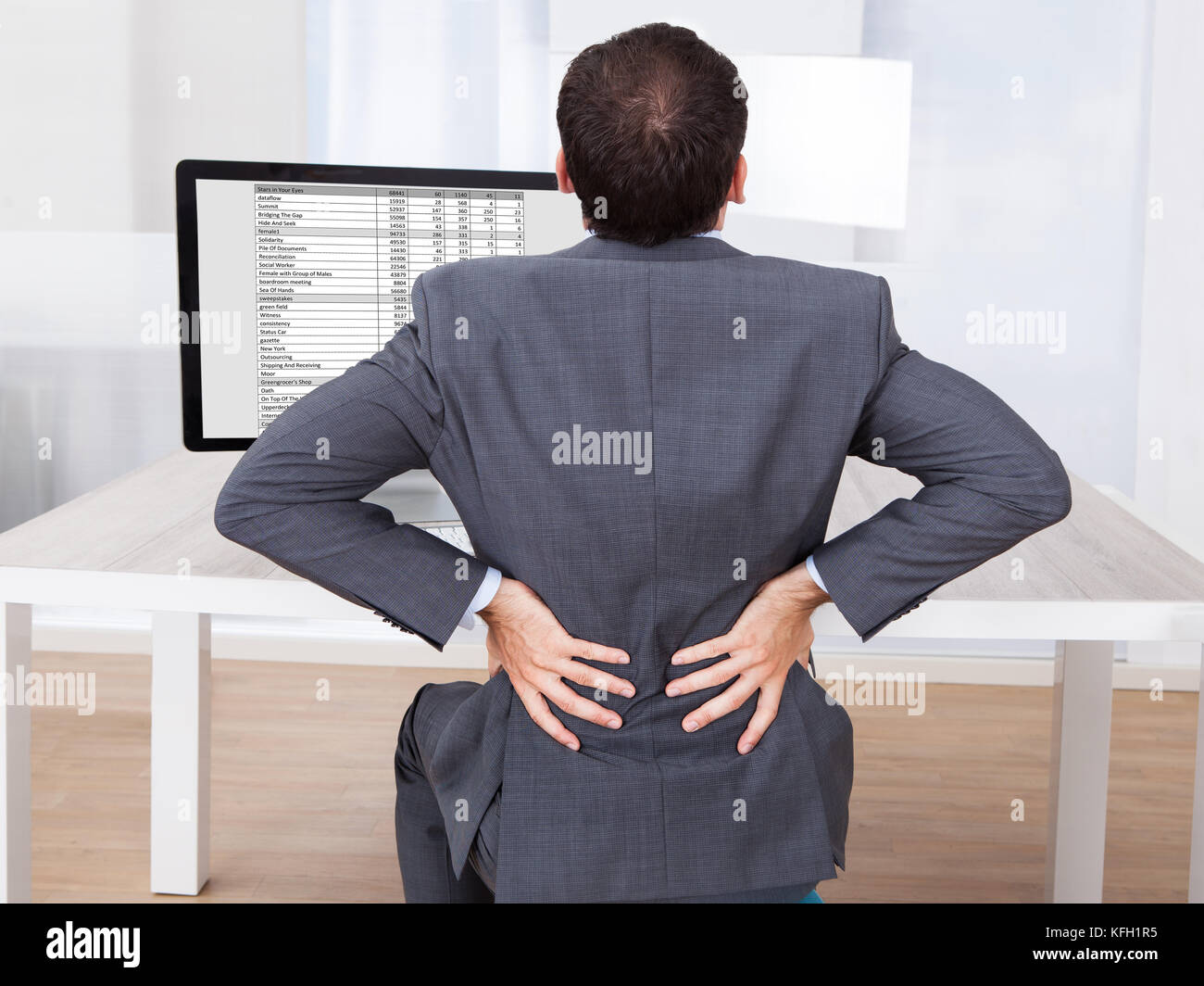 Rear view of businessman suffering from backache while sitting at ...
