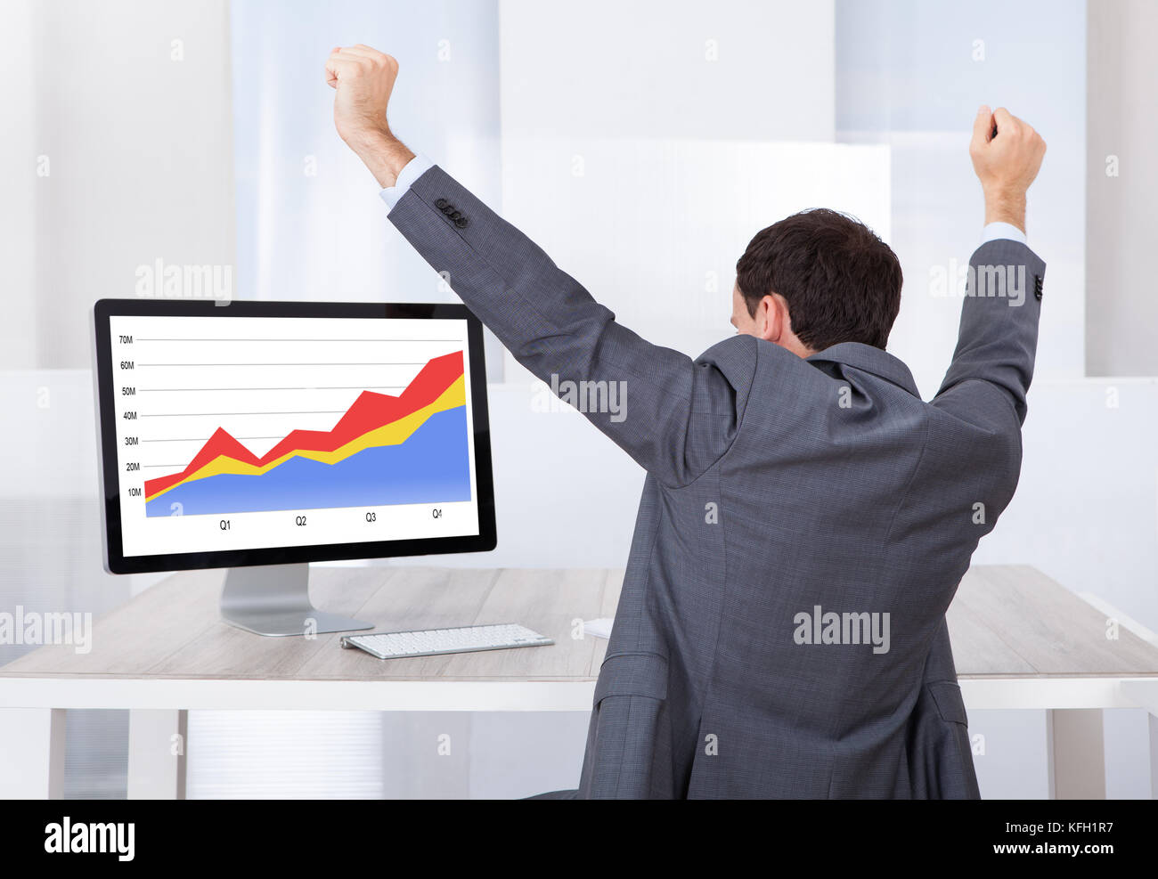 Rear view of businessman celebrating success at computer desk in office ...