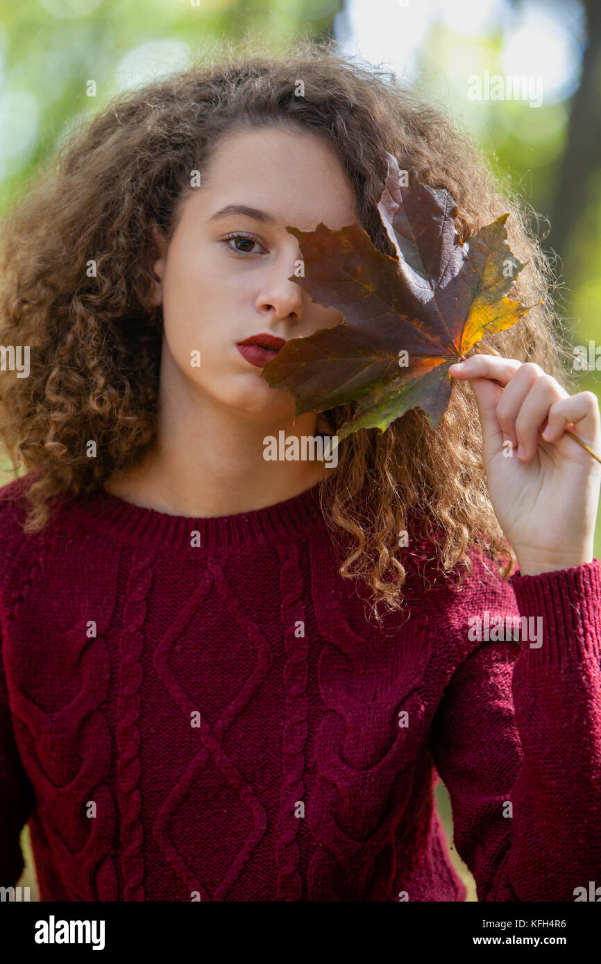 Portrait of curly hair teen girl holding maple leaf in autumn forest ...