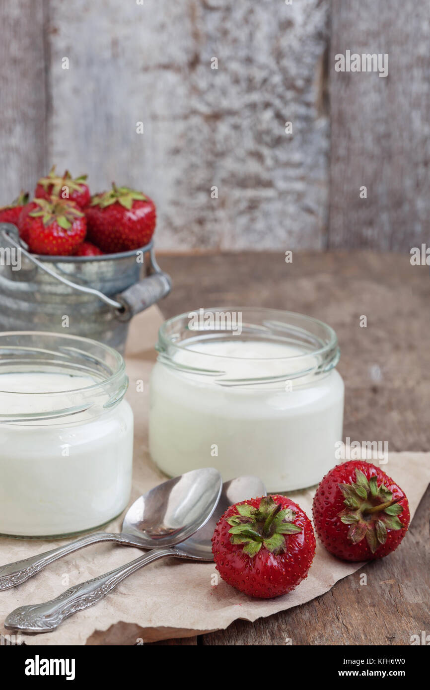 yoghurt in a glass and a bucket with fresh strawberries on a wooden ...