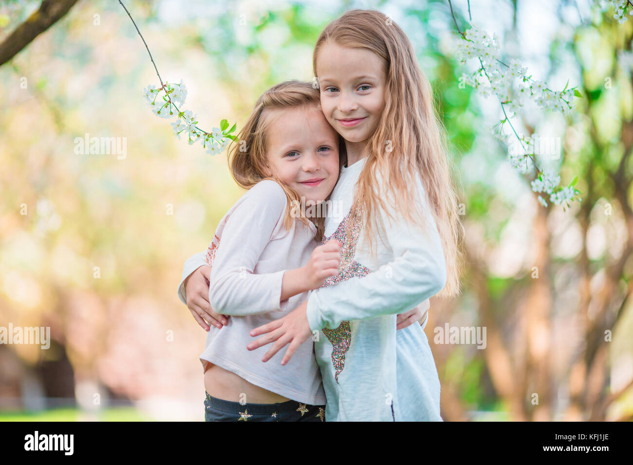 Adorable little girls in blooming cherry garden on beautiful spring day ...