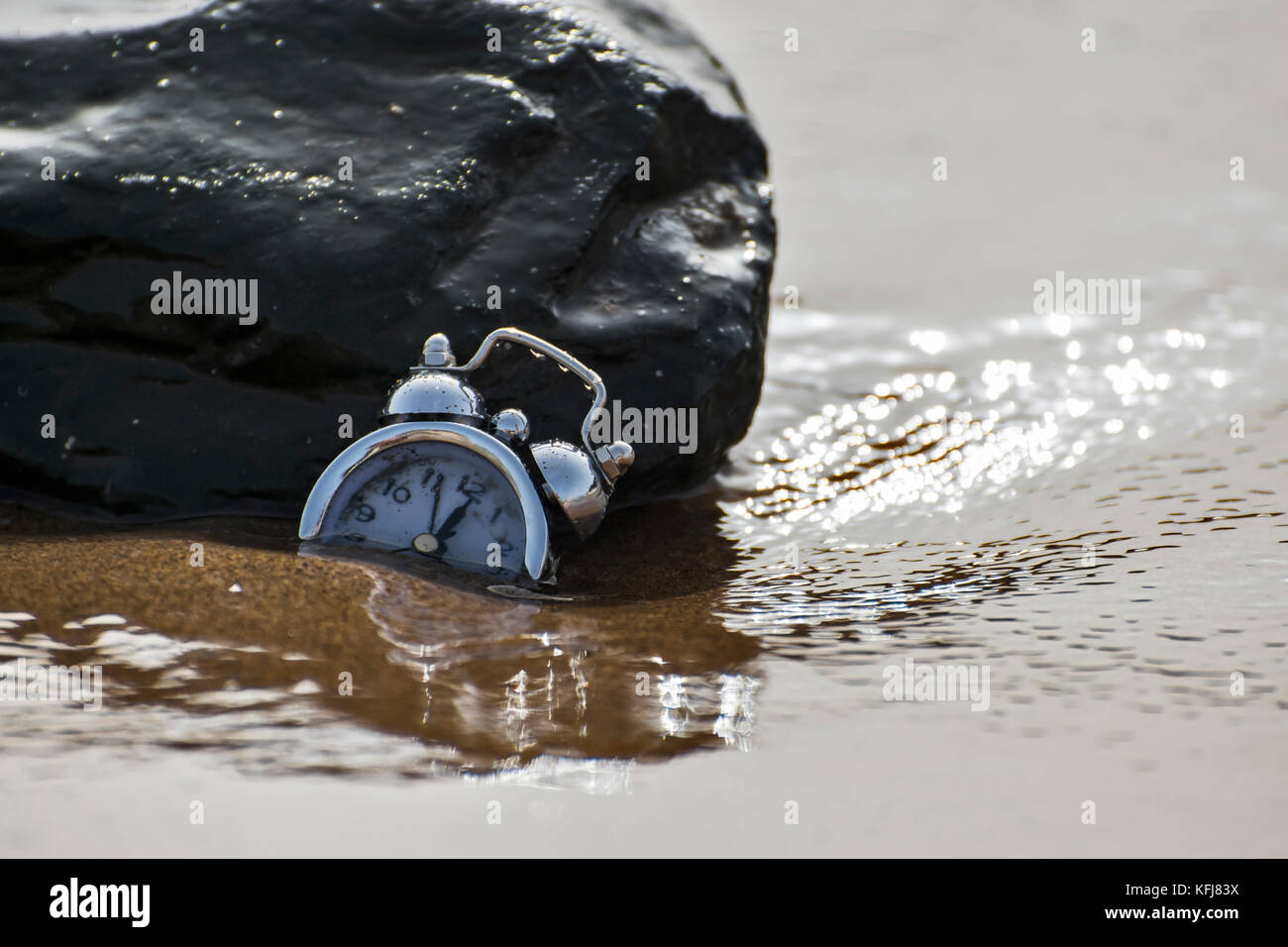 an abstract consept shot of a clock sinking in sand sorrounded by sea ...
