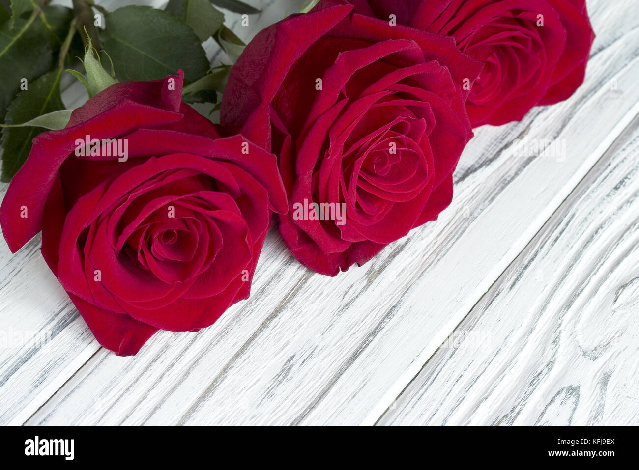 Three red roses on white wooden background Stock Photo - Alamy