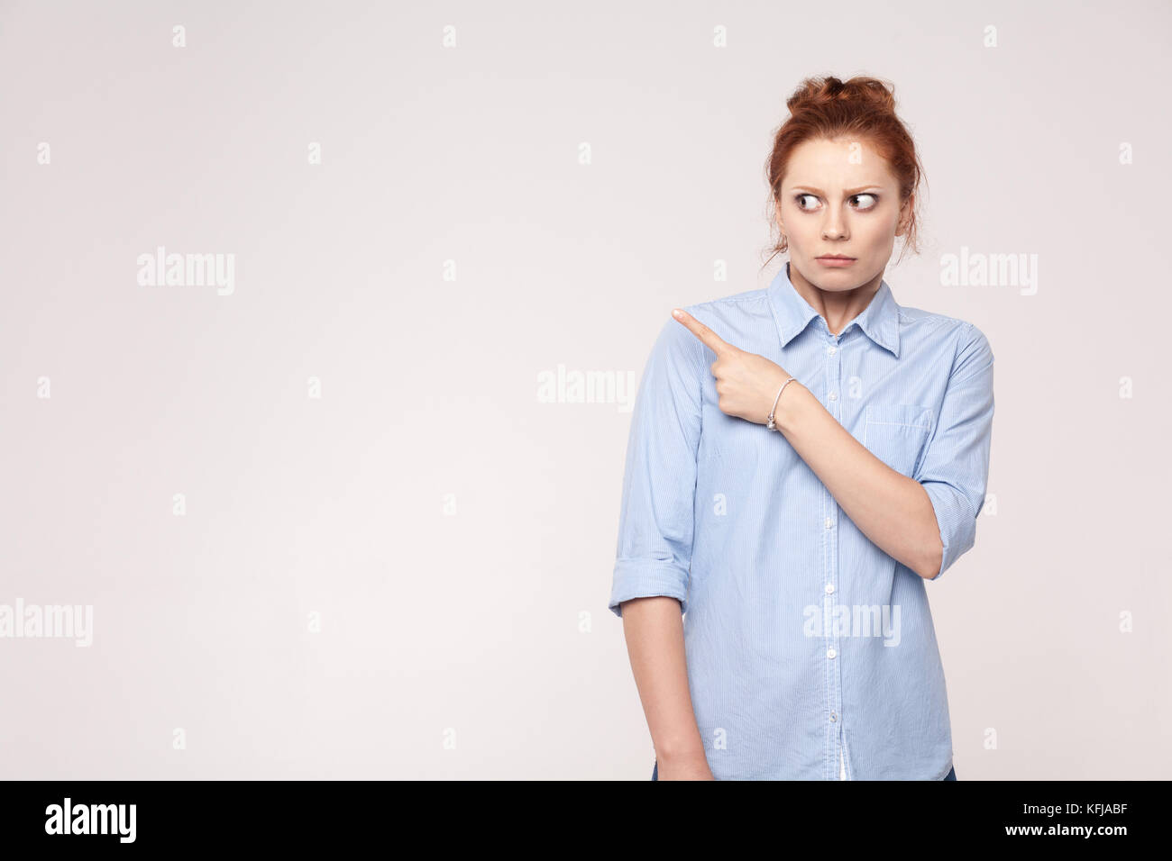 Scared redhead woman pointing away while standing isolated on gray ...