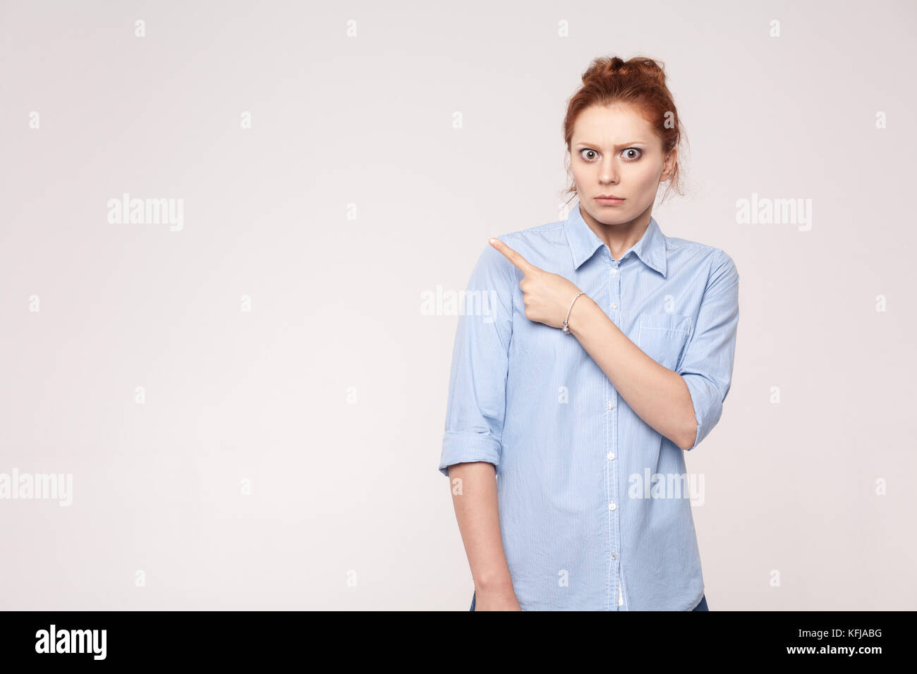 Scared redhead woman pointing away while standing isolated on gray ...