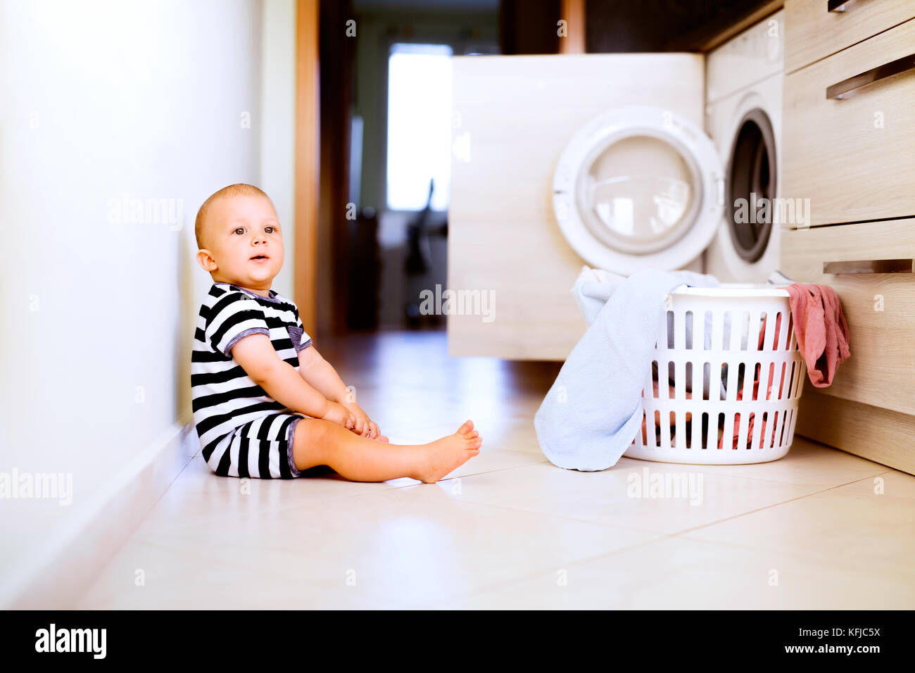 Baby boy by the washing mashine in the kitchen Stock Photo - Alamy