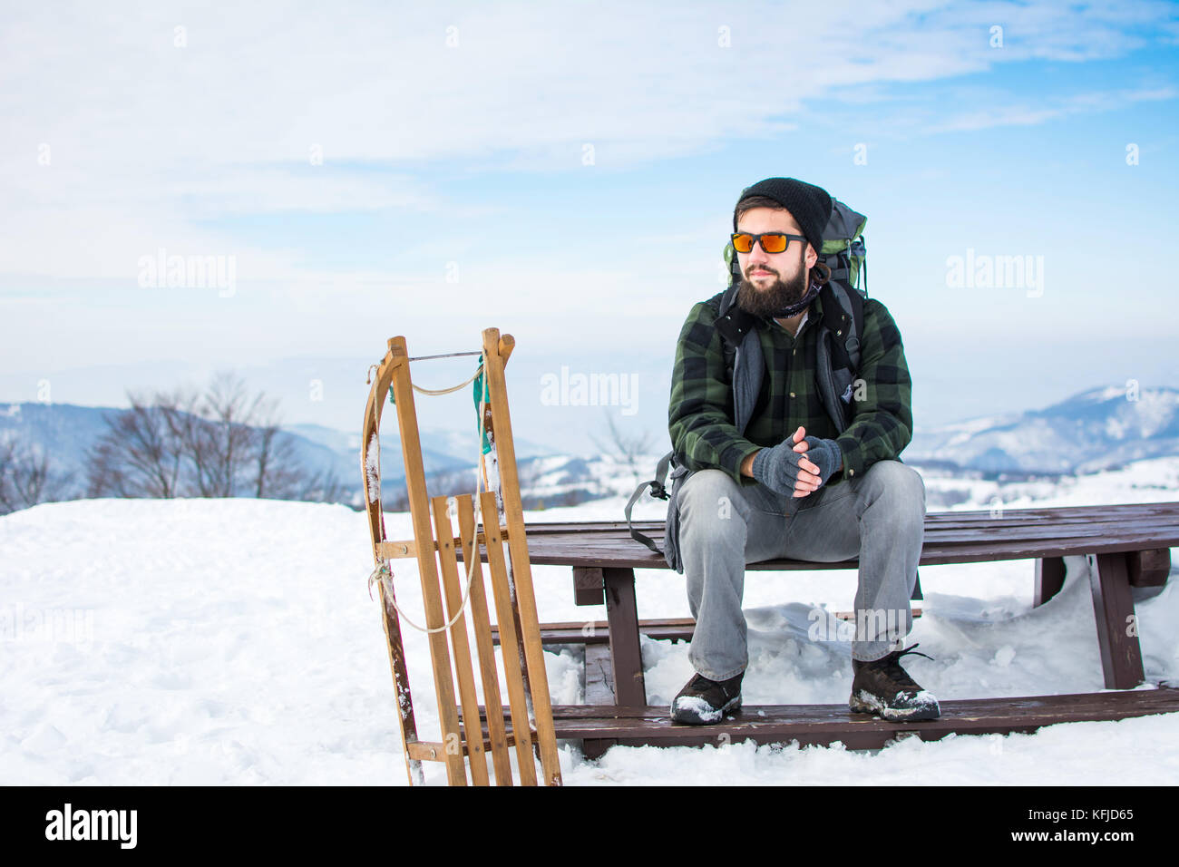 Man sitting on snowy mountain top with wooden sleds Stock Photo - Alamy