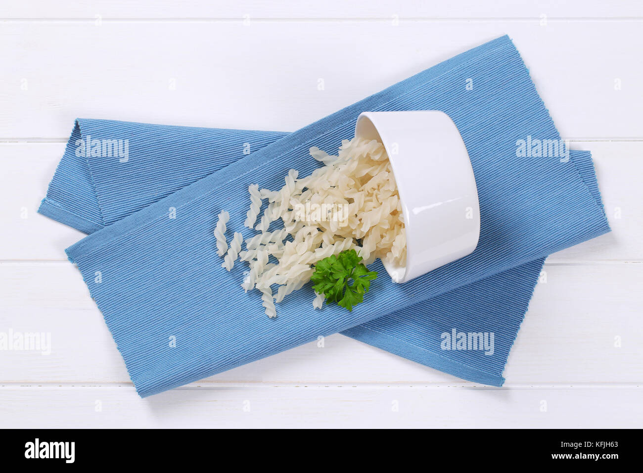 bowl of cooked rice pasta fusilli spilt out on blue place mat Stock ...