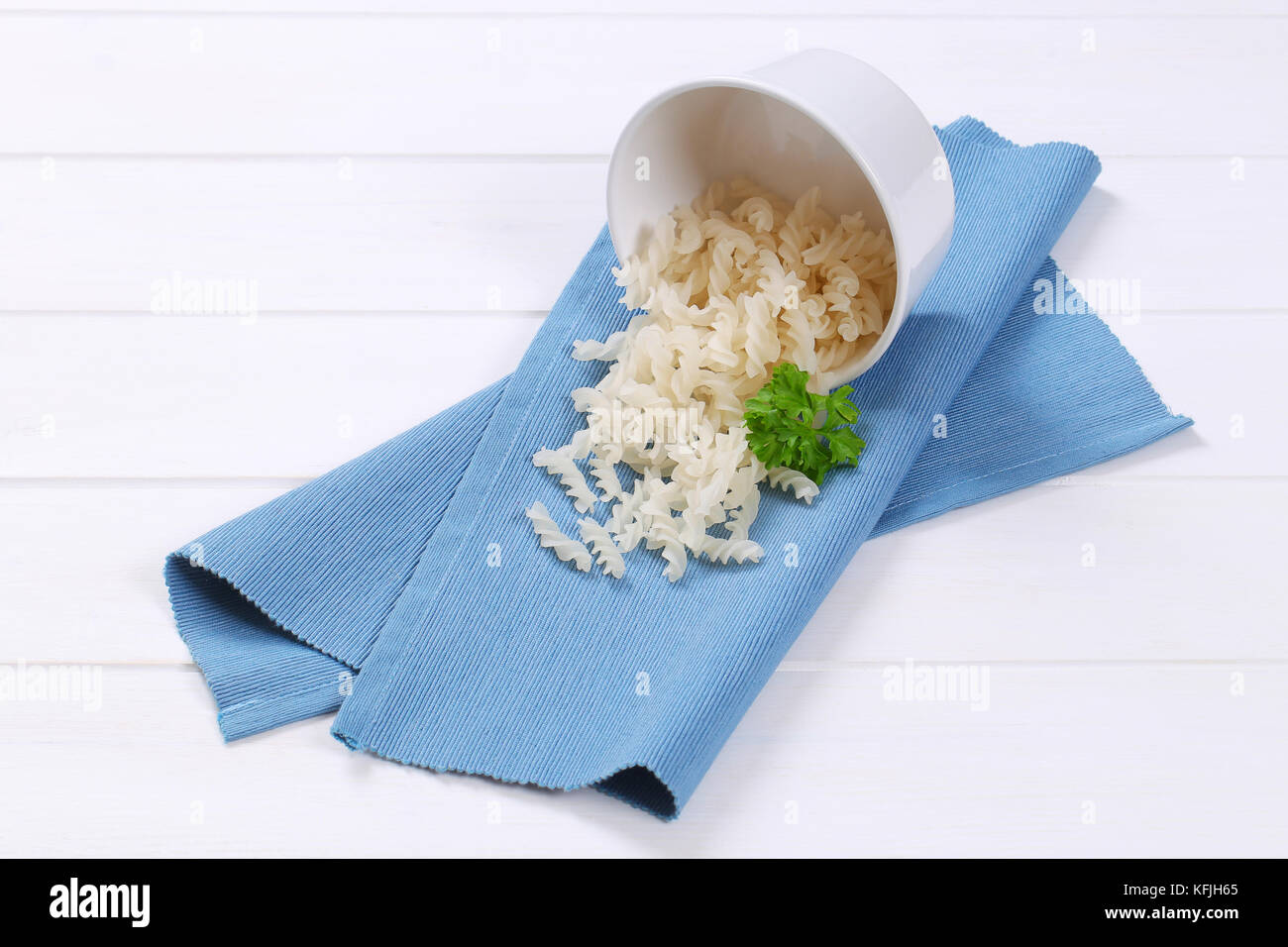 bowl of cooked rice pasta fusilli spilt out on blue place mat Stock ...