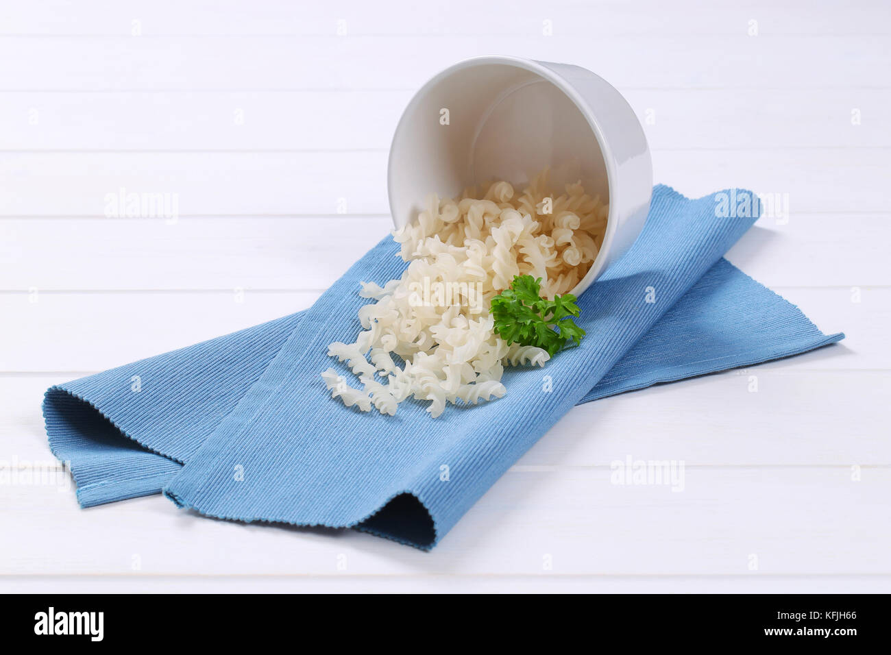 bowl of cooked rice pasta fusilli spilt out on blue place mat Stock ...