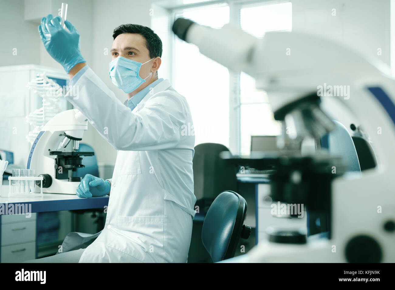 Serious medical worker looking at test tube Stock Photo - Alamy