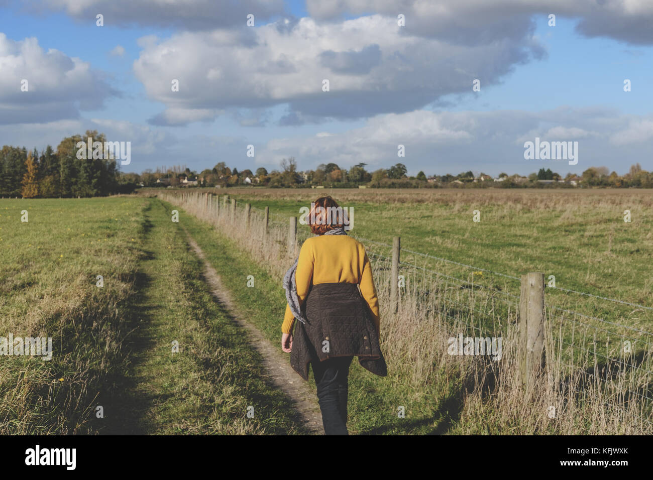 Woman walking alone along a country footpath, adjacent to open fields ...
