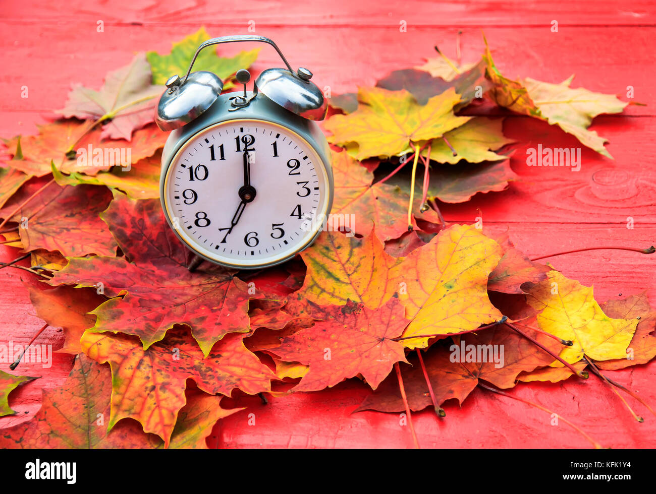 old metal clock standing on a red wooden table amongst fallen autumn ...