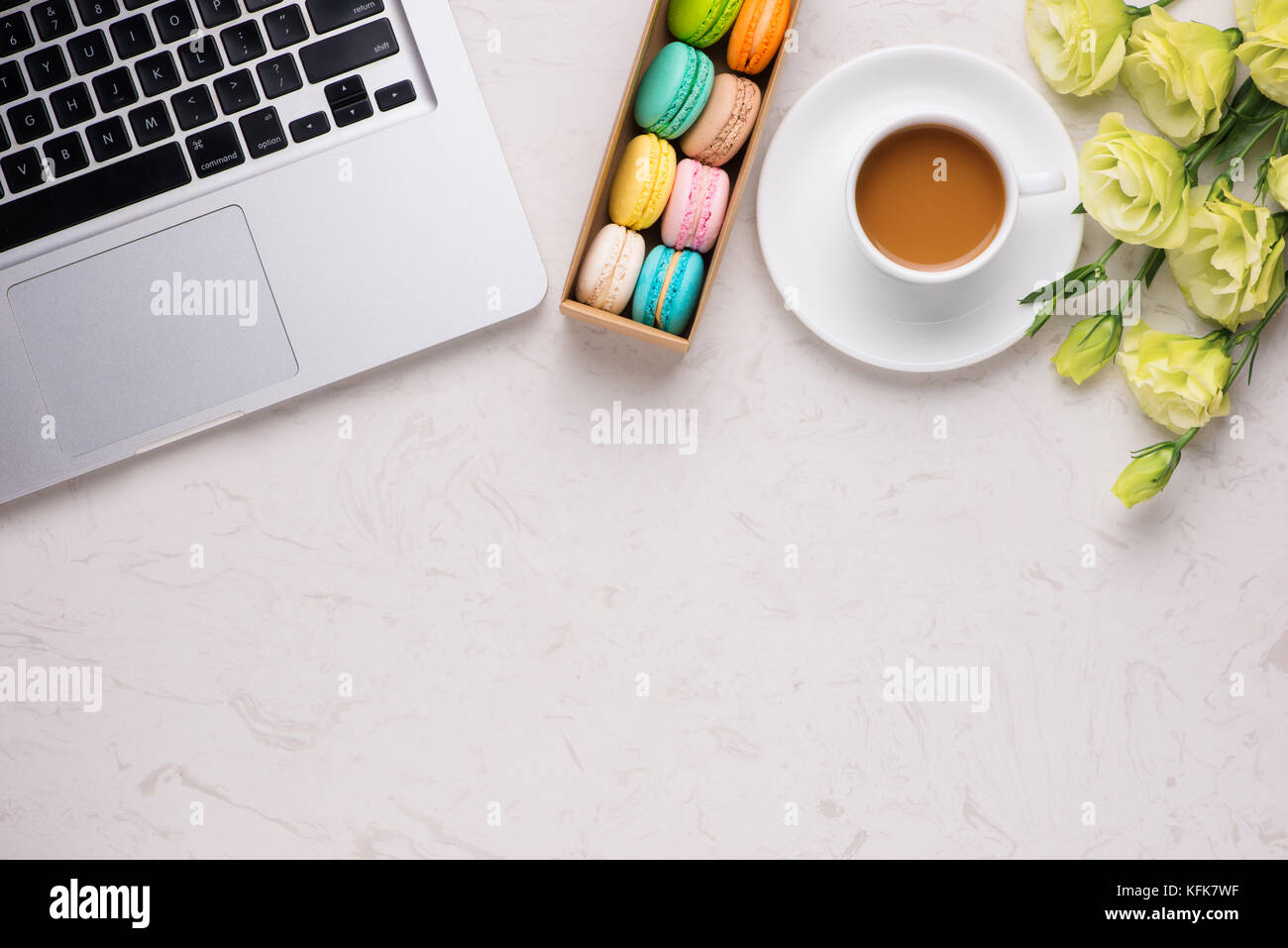 White desk with colorful macaroons, flowers, notebook, laptop and cup ...