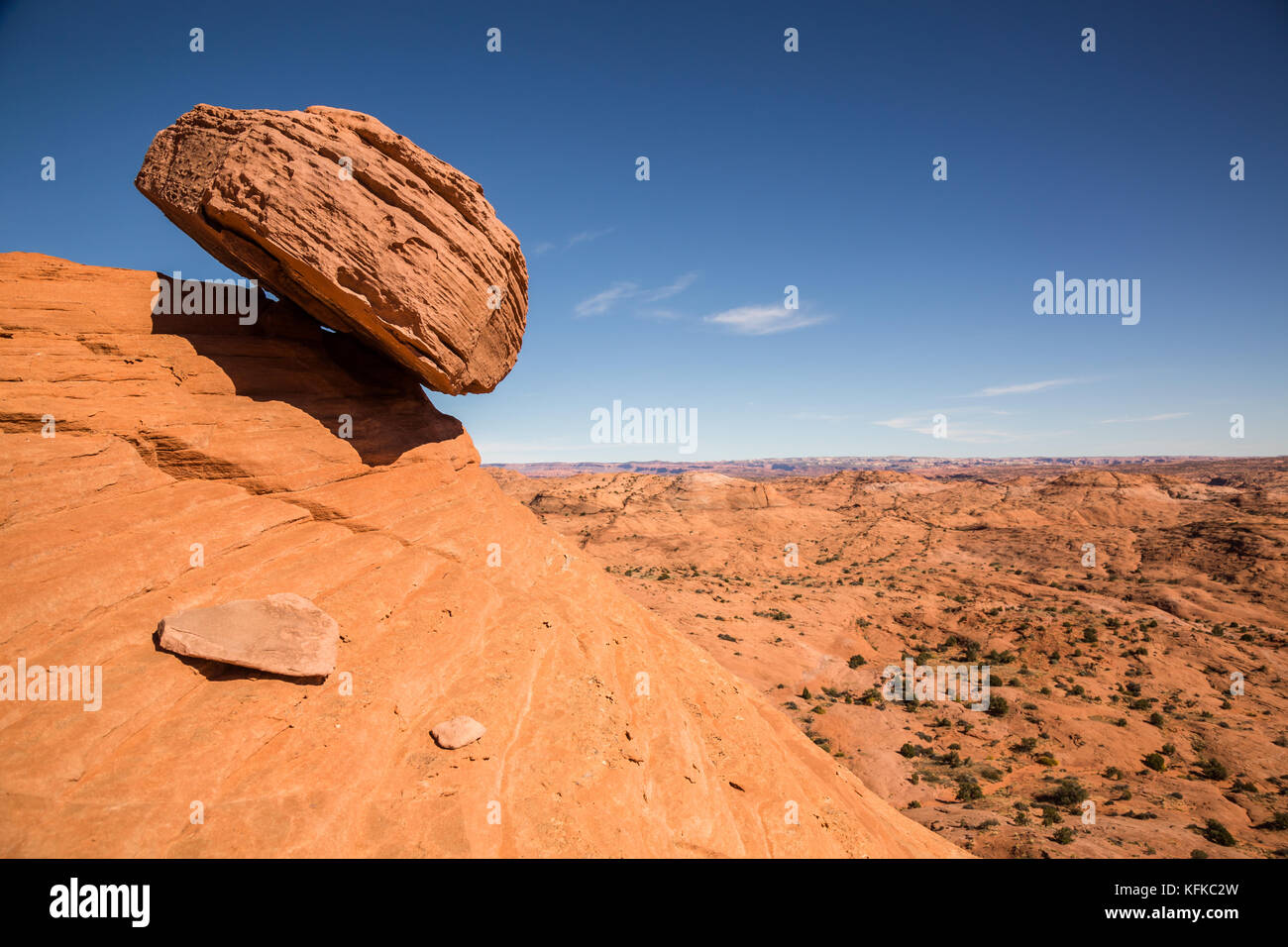 A large sandstone boulder rests precariously over a slope in the desert ...