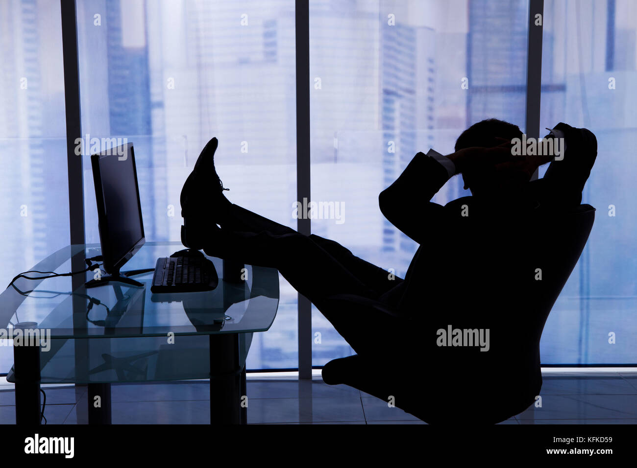 Relaxed businessman sitting with feet up at computer desk in office ...