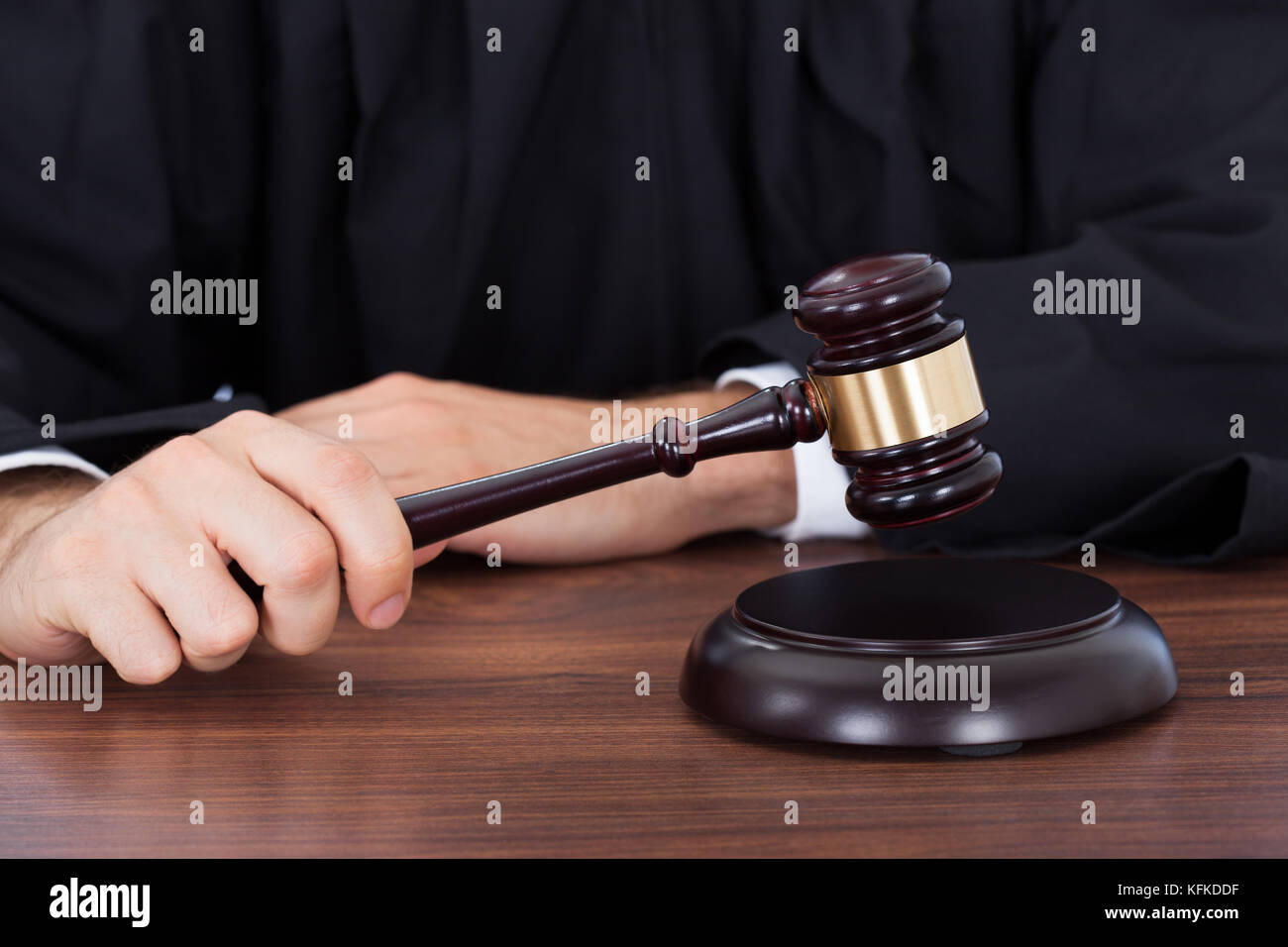 Midsection of male judge striking gavel on block at desk in courtroom ...